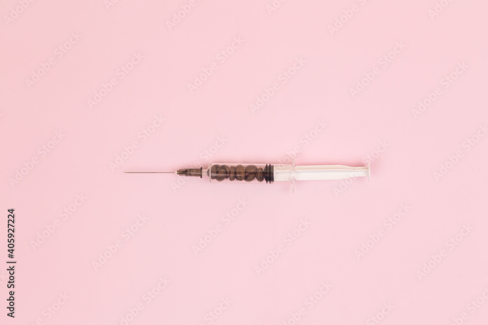 Transparent syringe with coffee beans inside on a pink background. View ...