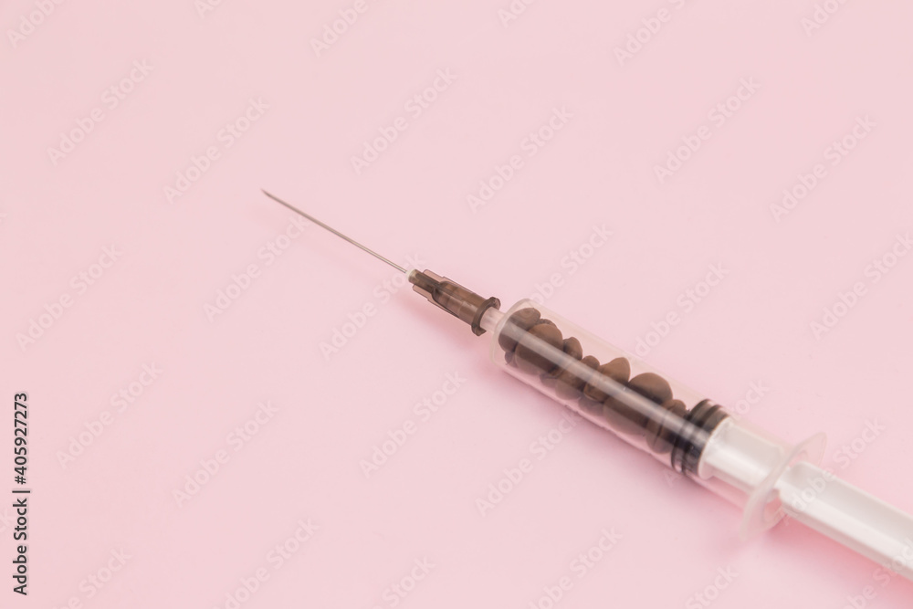 Transparent syringe with coffee beans inside on a pink background. View ...
