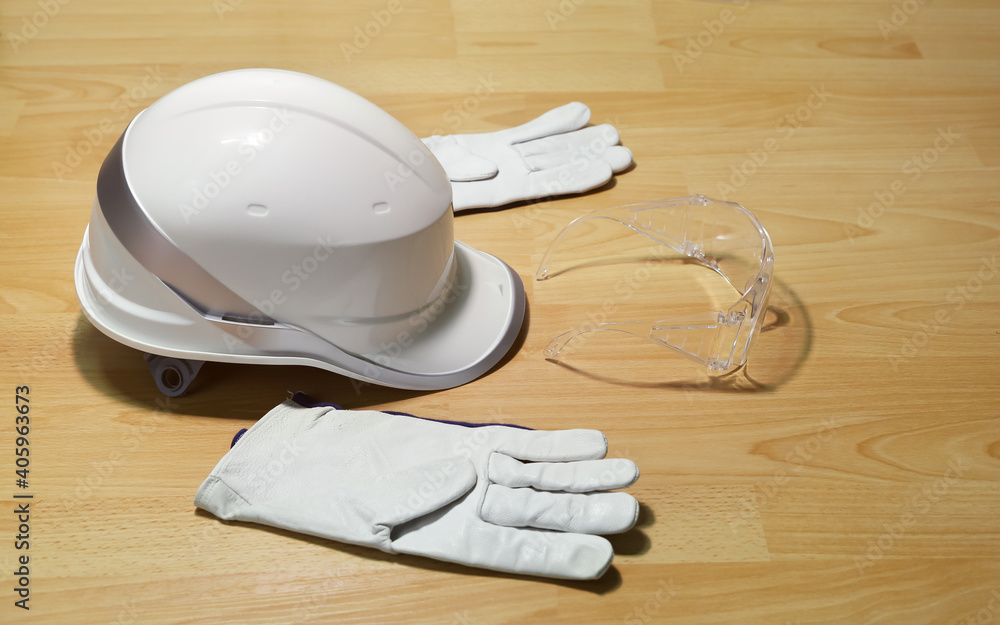 White construction helmet, safety goggles and leather gloves on surface ...
