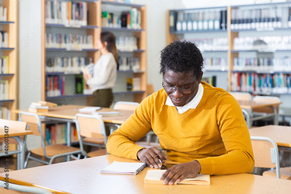 Adult male student working in library, reading and writing notes ...