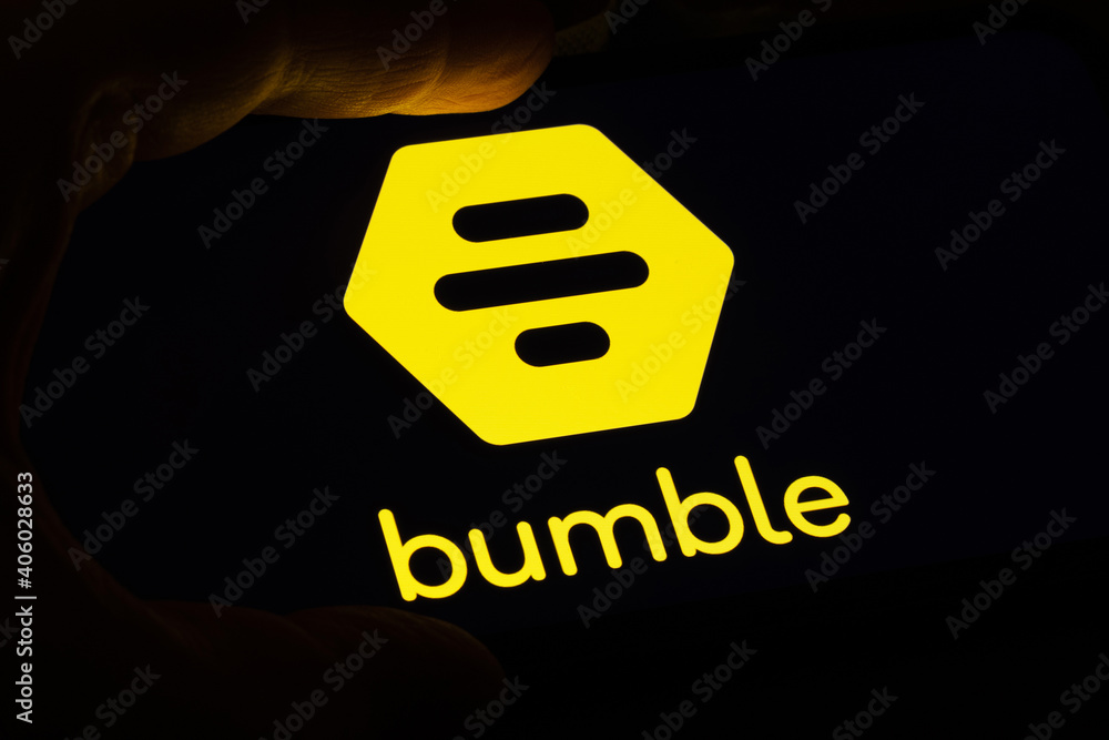 Hand holding a smartphone with a Bumble dating icon on screen at night ...