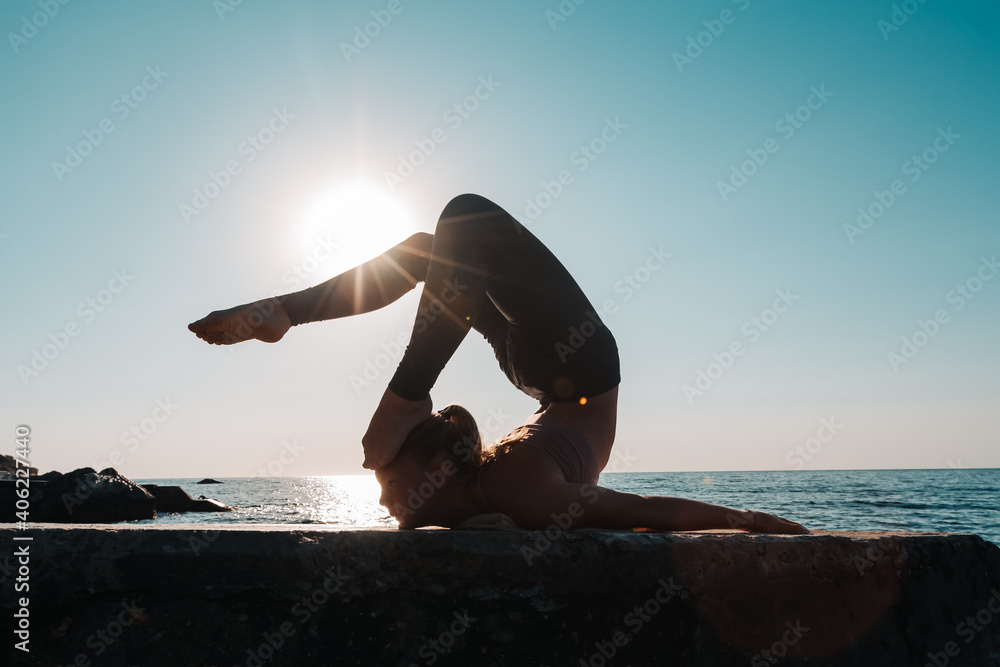 Advanced yoga - teenage girl makes scorpion pose by sea in sun. Woman ...