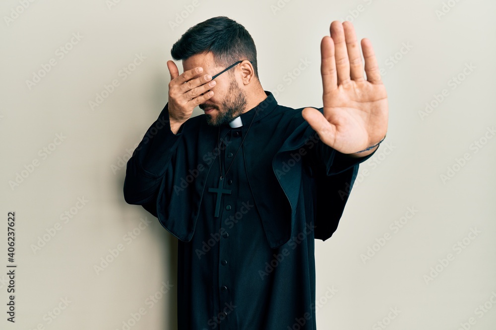 Young hispanic man wearing priest uniform standing over white ...