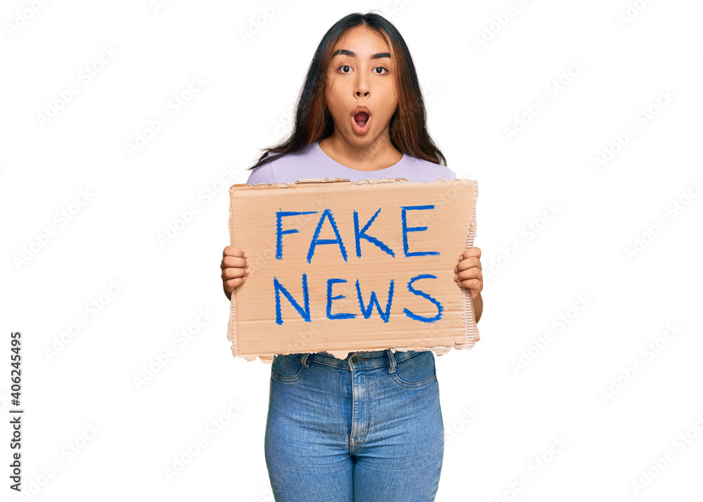 Young latin woman holding fake news banner scared and amazed with open ...