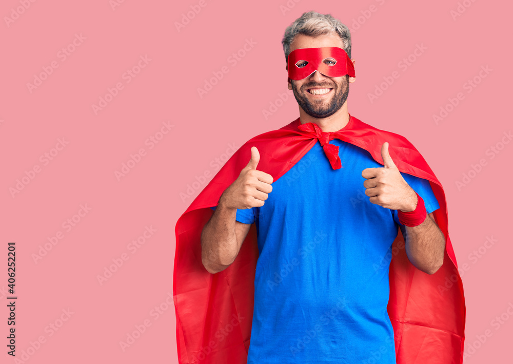 Young blond man wearing super hero custome success sign doing positive ...