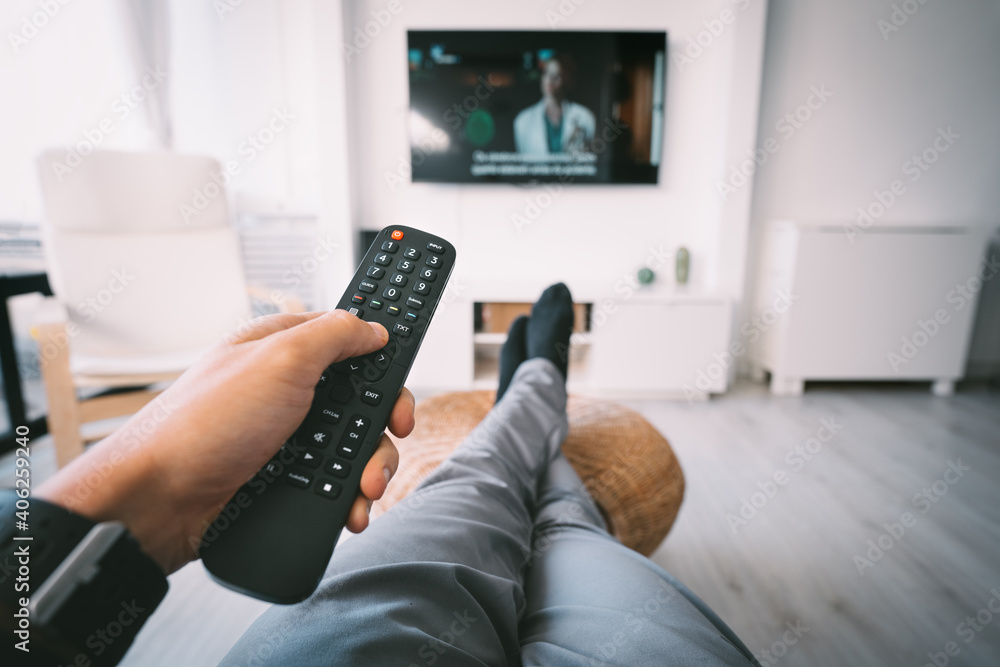Man sitting on sofa and watching TV with remote controller in his hand ...