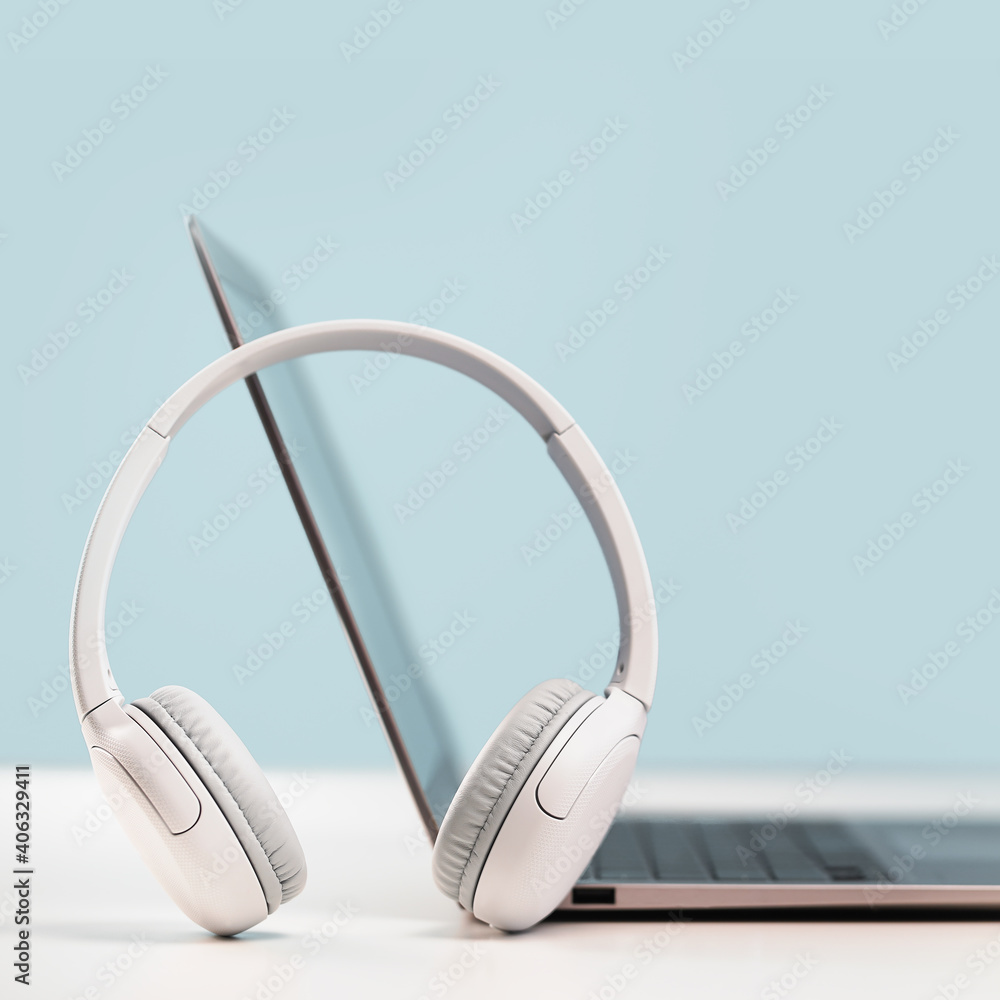 Side view of slim laptop with wireless headphones on grey desk. Blue ...