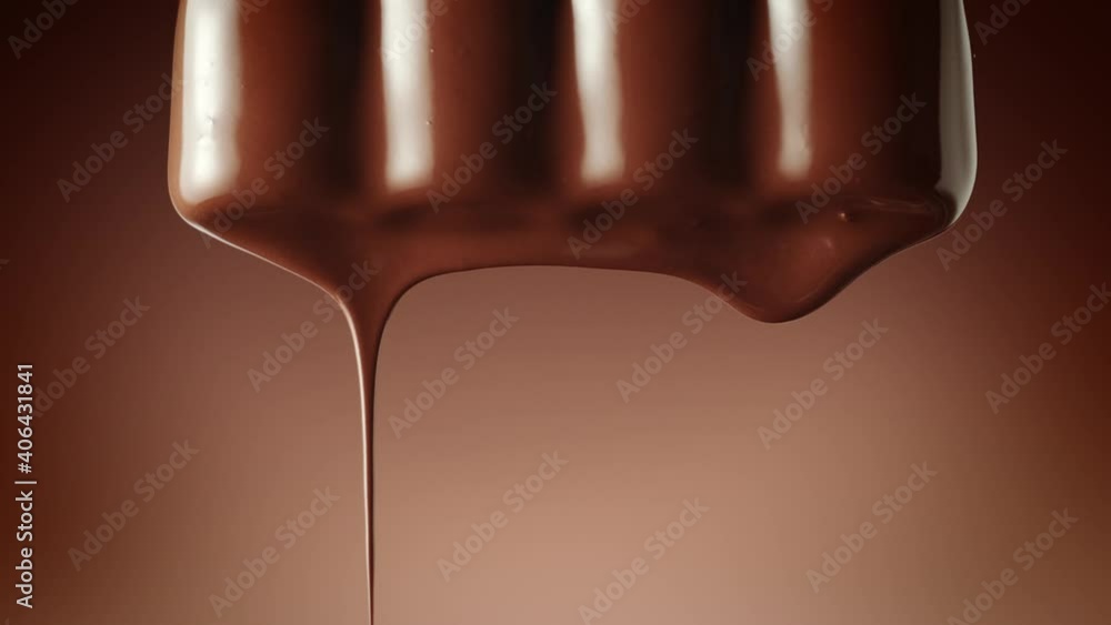 Melted chocolate dripping from a chocolate bar over a dark brown ...