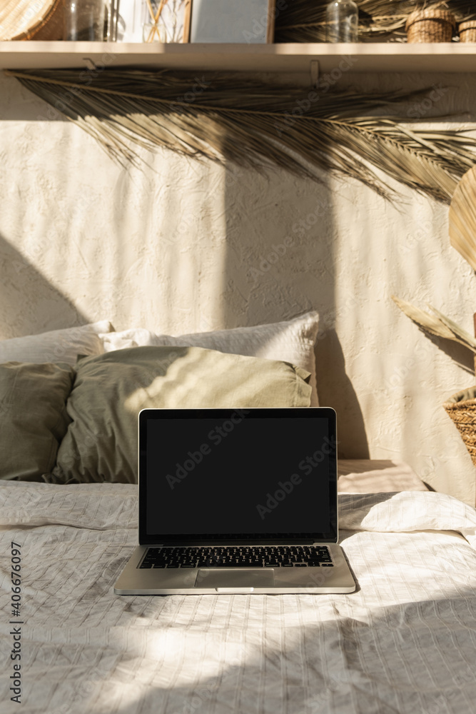 Blank screen laptop in bed with pillows and linens. Boho style home ...