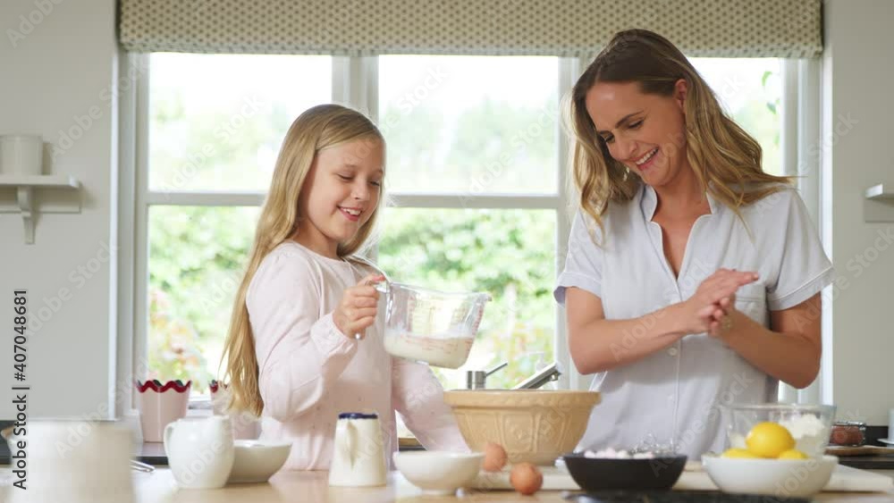 Mother wearing pyjamas in kitchen putting mixture on daughter's nose as ...