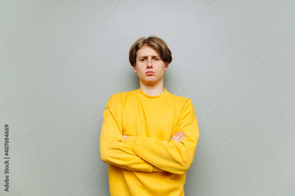 Dissatisfied young man in yellow clothes stands on a gray background ...