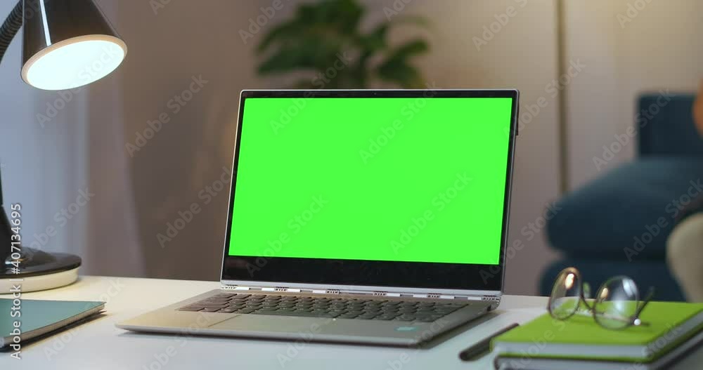 open laptop with green screen on working table in living room, man is ...