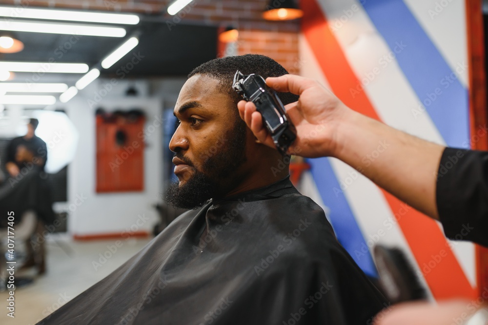 Portrait of young black man being trimmed with professional electric ...