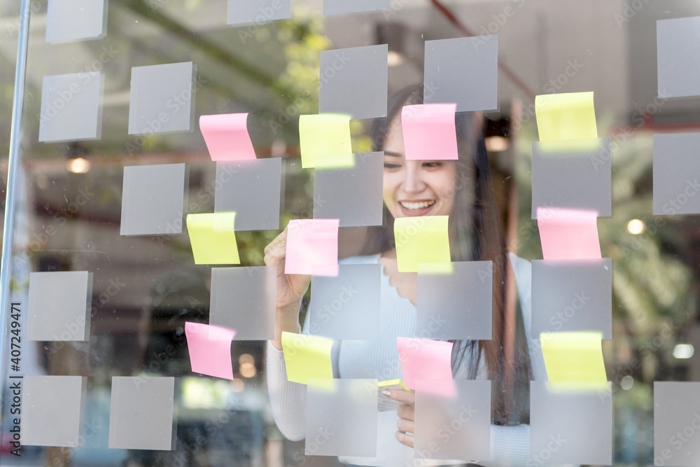 Professional women use post-it notes in a glass wall to write business ...
