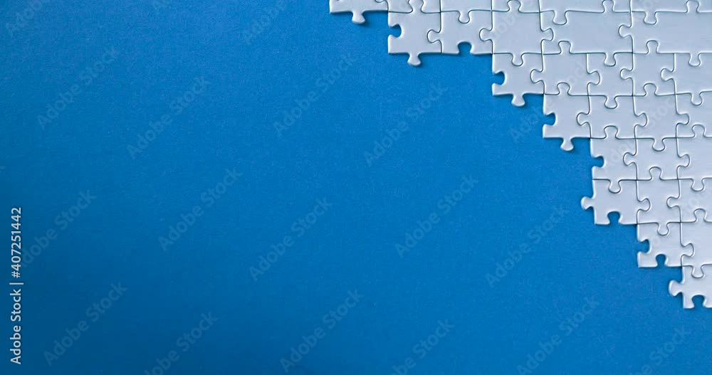 Gray puzzles stacked on blue background. Female hand is putting down ...