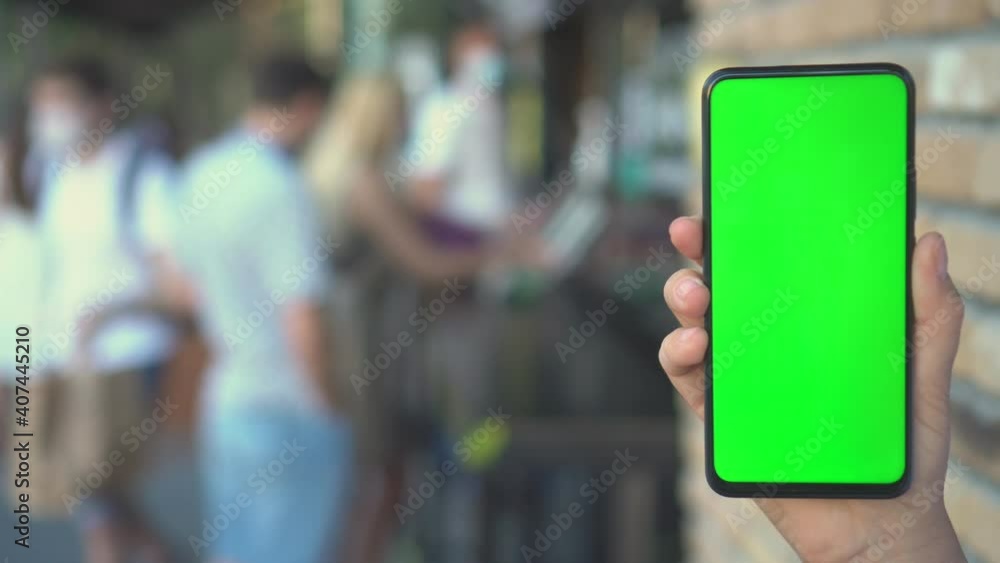 Close up hands woman holding phone with vertical green screen on busy street background pavement ...