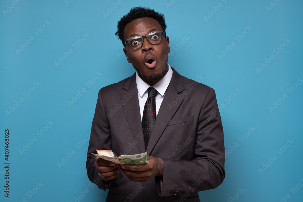African man in suit holding and counting money. Studio shot on blue ...