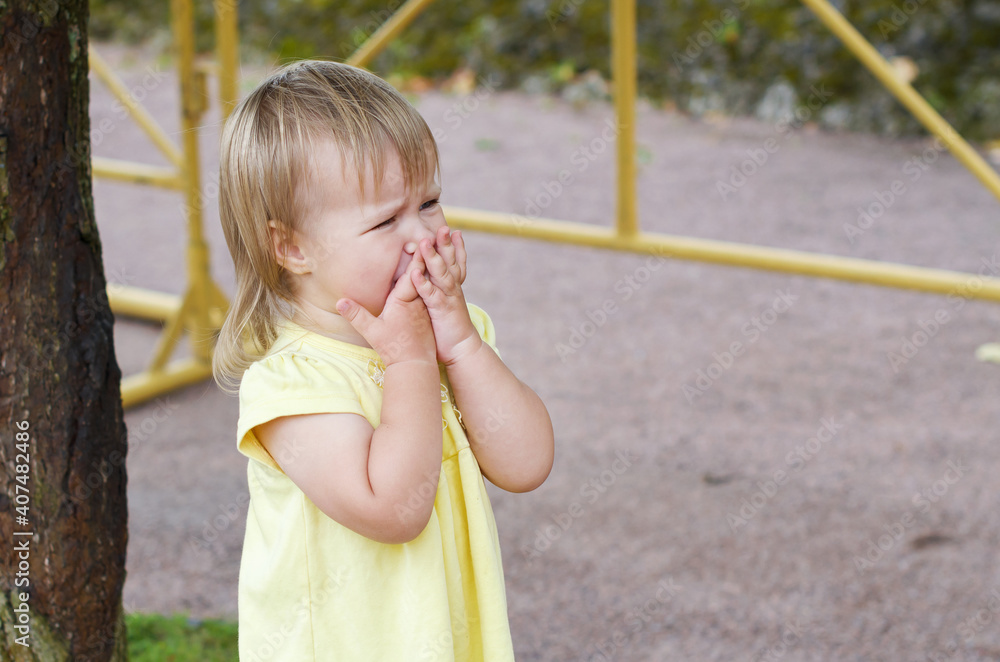 Little blonde baby girl in a yellow dress crying in the park. Sad ...