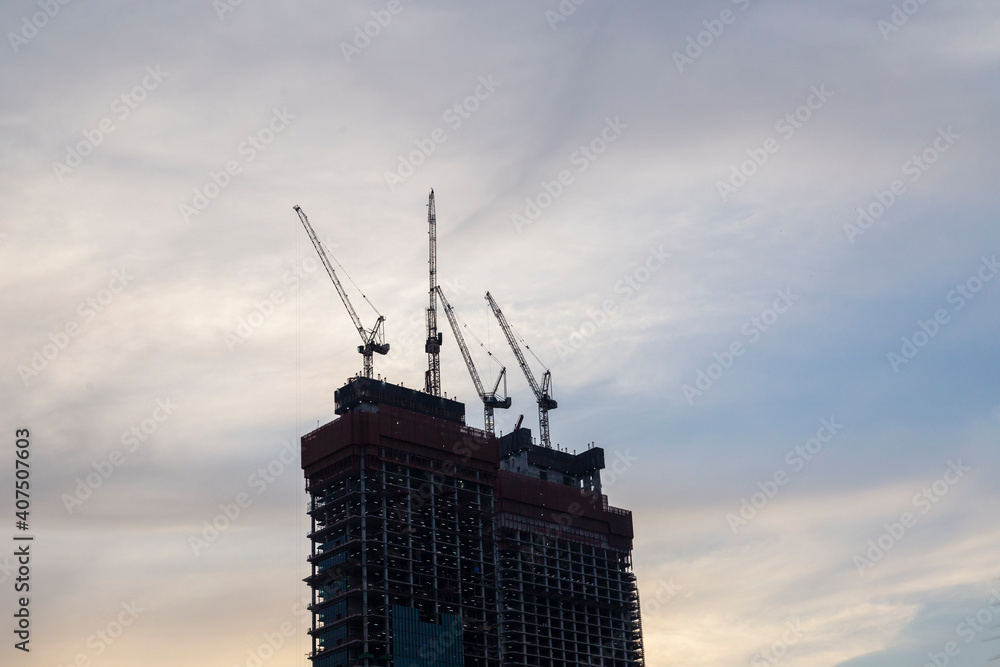 Tower cranes in action at construction site on sunset background. Crane ...
