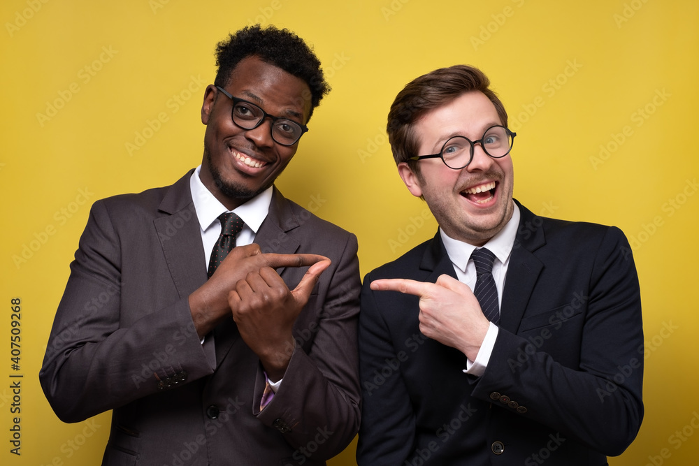 Two young african and caucasian men pointing finger each other and ...