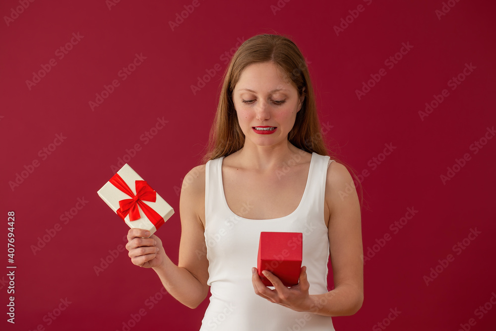 Embarrassed woman looking on a present on red background Dissappointed ...