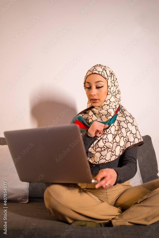 Arab girl with a white veil on her home computer on the sofa in her ...