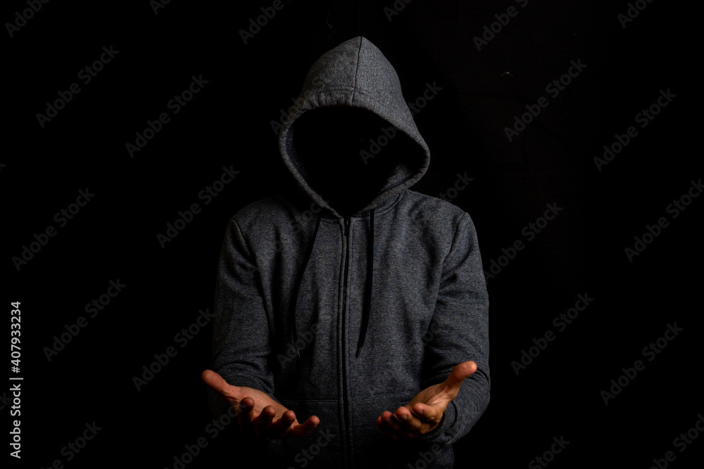 Man without a face in a hood holds something in his hands on a dark ...