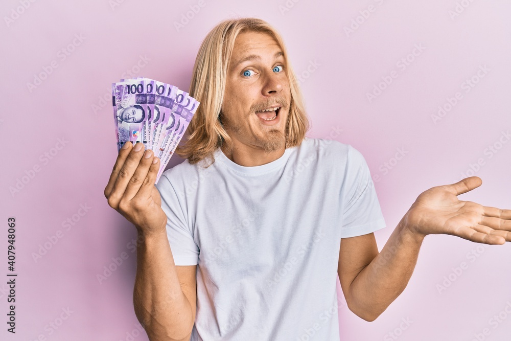 Caucasian young man with long hair holding 100 philippine peso ...