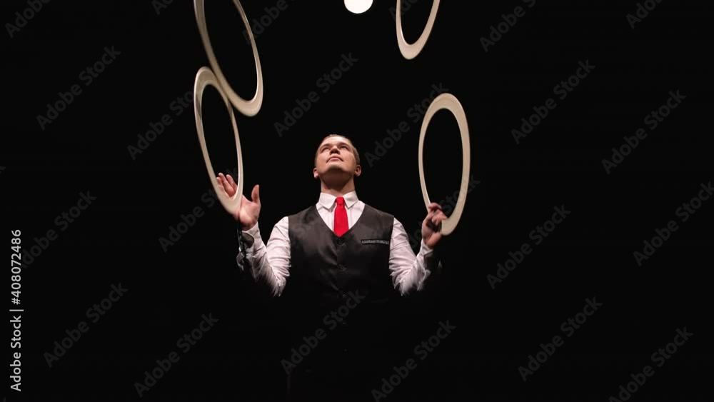 Camera rotates around concentrated man juggling white rings, then puts ...