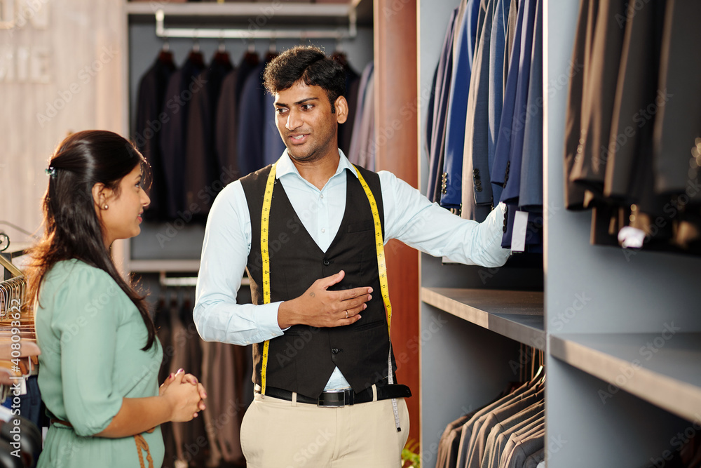 Shop assistant showing young woman assortment of jackets and male suit ...
