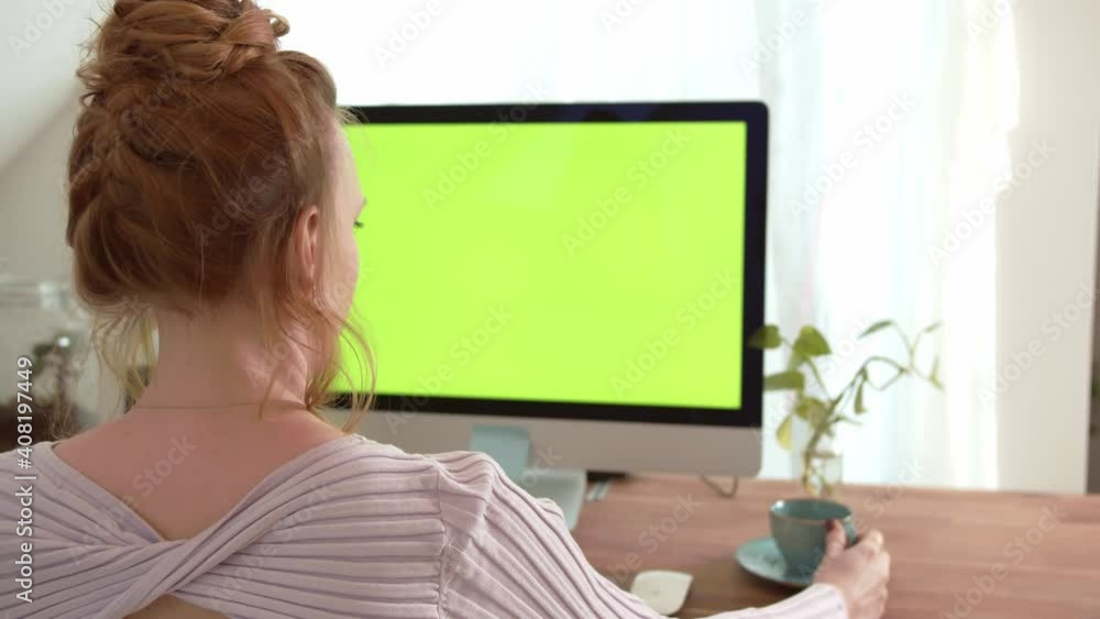 Young women sitting in front of computer with green screen mock-up ...