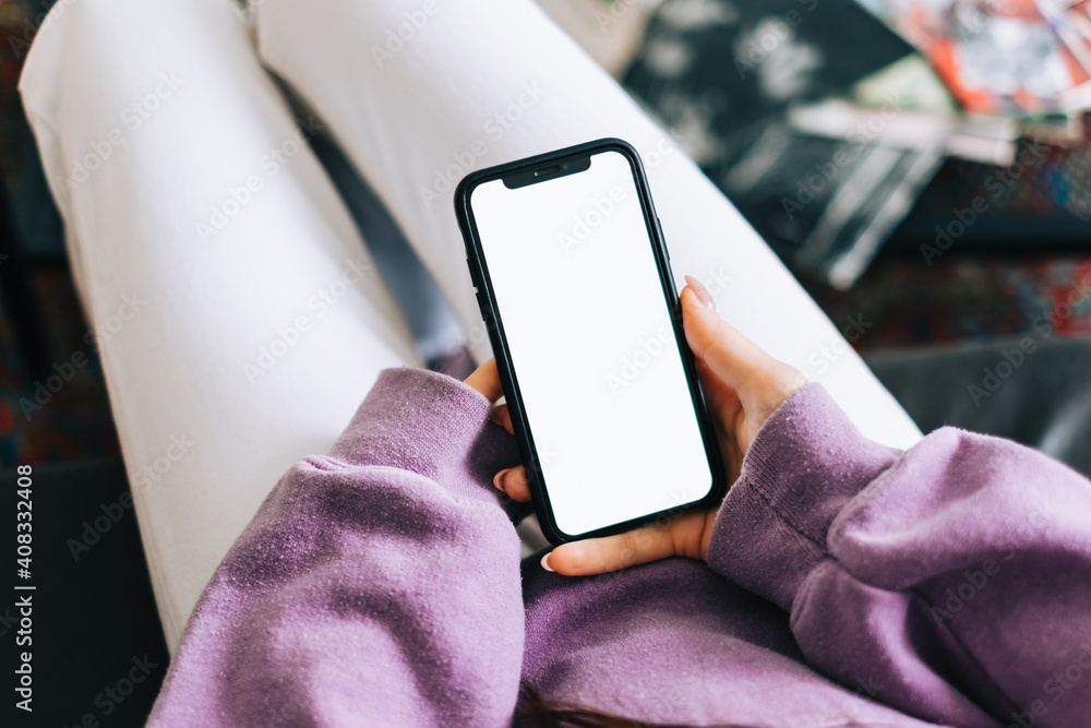 Woman holding a smartphone with a white screen mock up, sitting on the ...