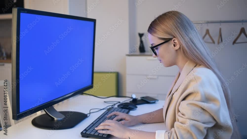 A beautiful girl looks into a large monitor and prints something. Woman ...