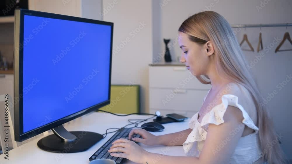 A beautiful girl looks into a large monitor and prints something. Woman ...