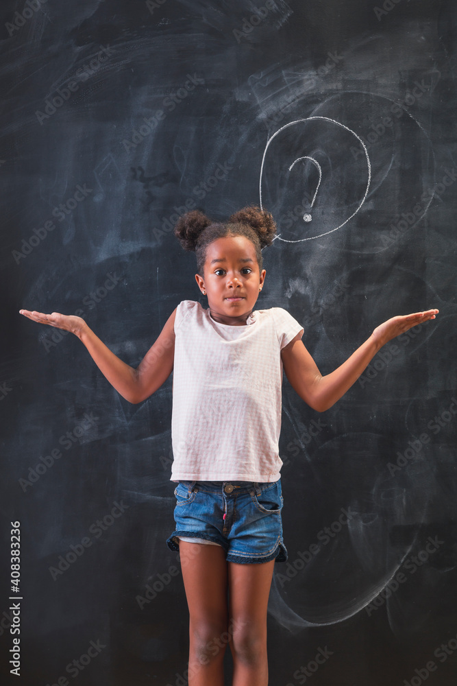 Child standing confused in front of a chalkboard, wondering with ...