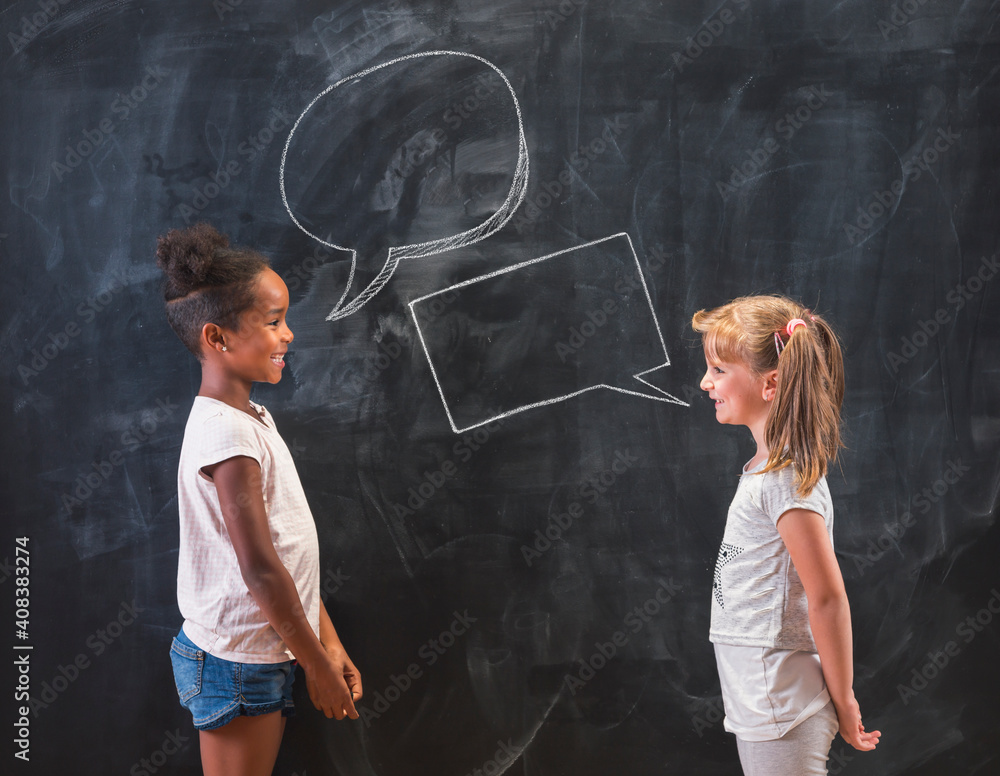 Two little girls having a debate in front of blackboard in classroom at ...