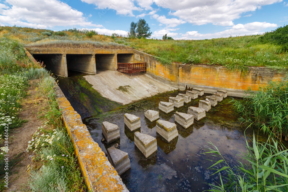 Concrete discharge sluice in earthen dam on small river in countryside ...