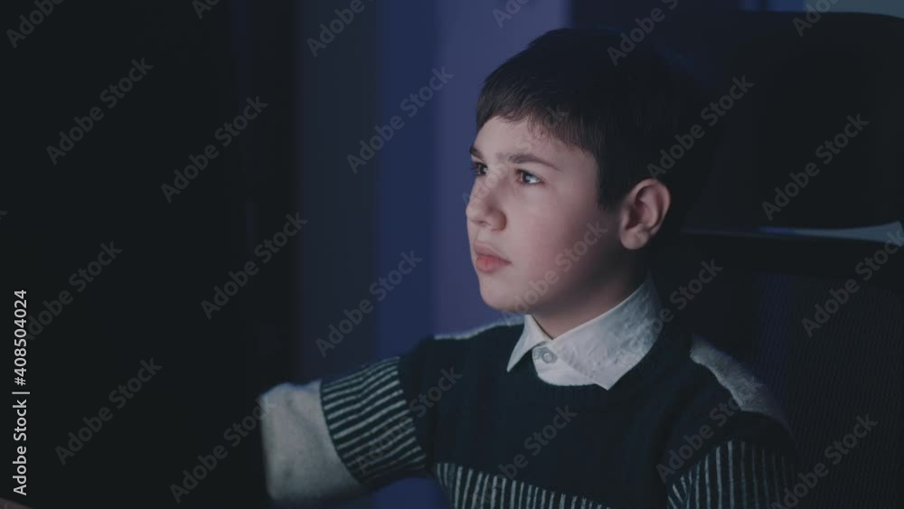 12-13 year old boy uses computer at night home. Child learning online ...