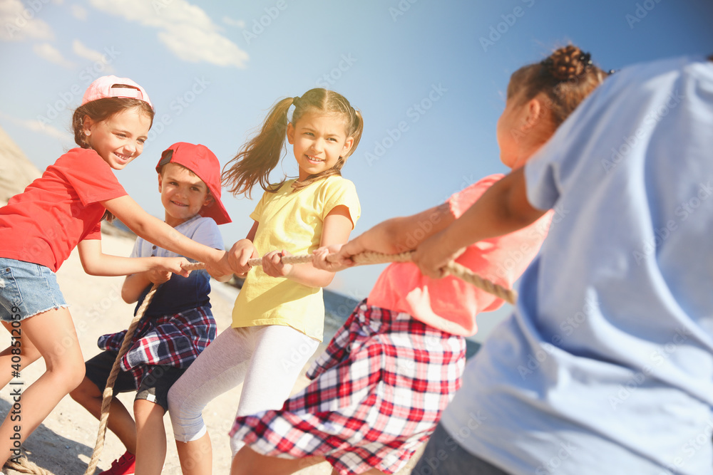 Cute children pulling rope during tug of war game on beach. Summer camp ...