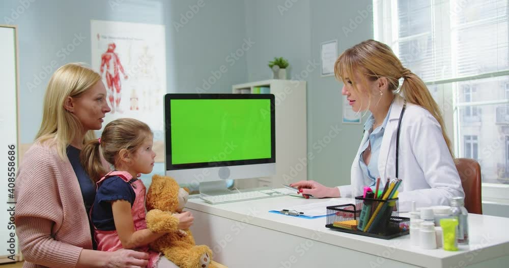 Medium shot of female pediatrician showing computer with green screen ...