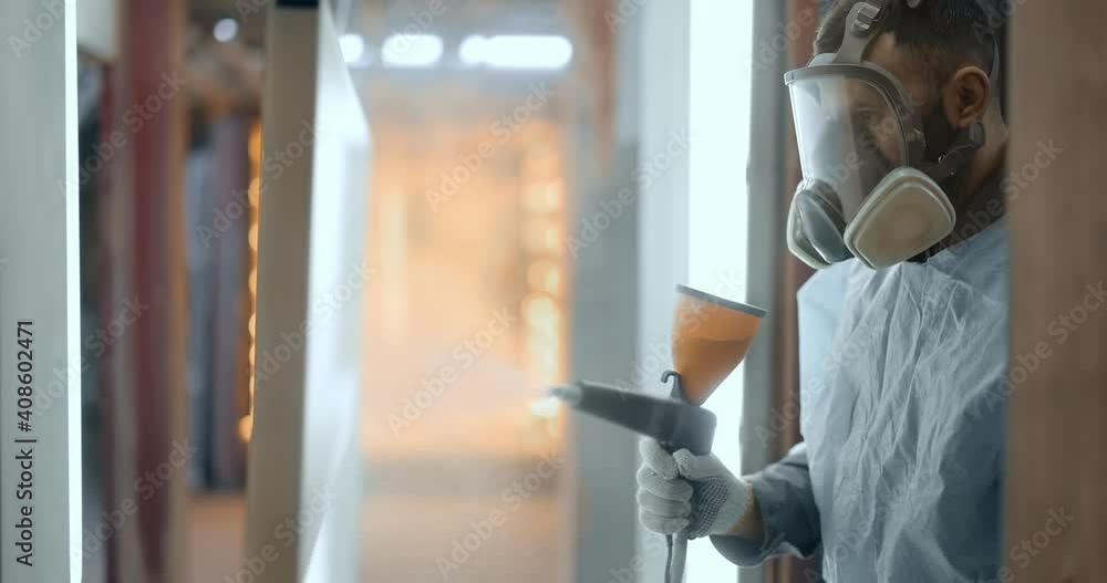 Painter in protective wear paints metal products with powder paint ...