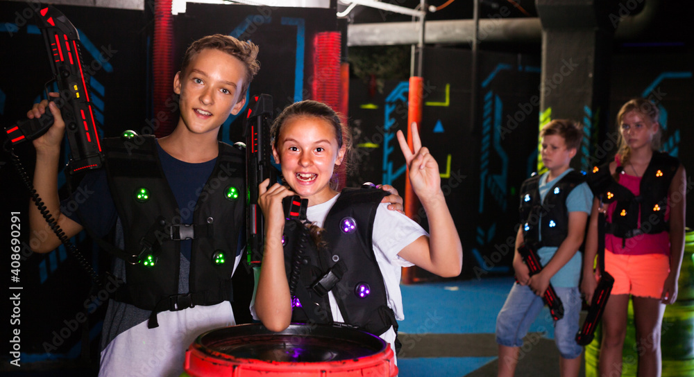 Cheerful teen girl and boy with laser pistols posing together in laser ...
