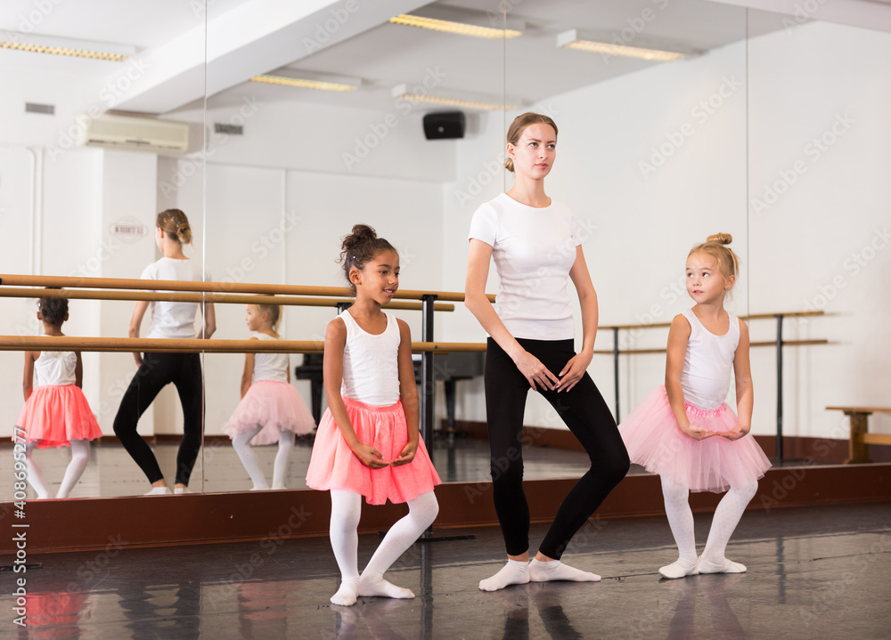 Young female ballet teacher and two little girls in classical dance ...