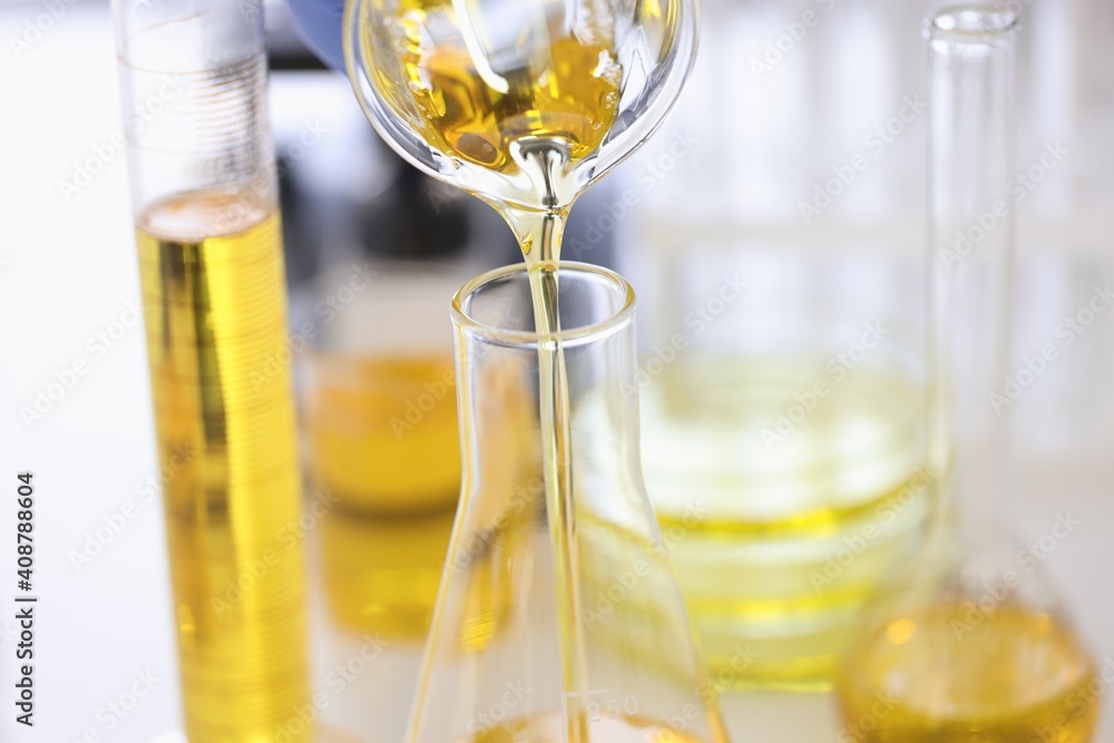 Yellow liquid flowing from test tube to flask in laboratory closeup ...