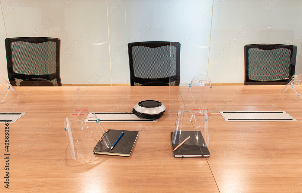 Close up face shield and notebook on table in meeting room with clear ...