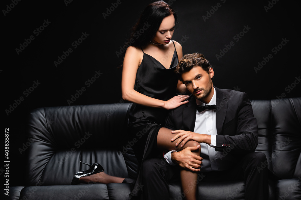 elegant man hugging leg of sexy woman while sitting on leather sofa ...