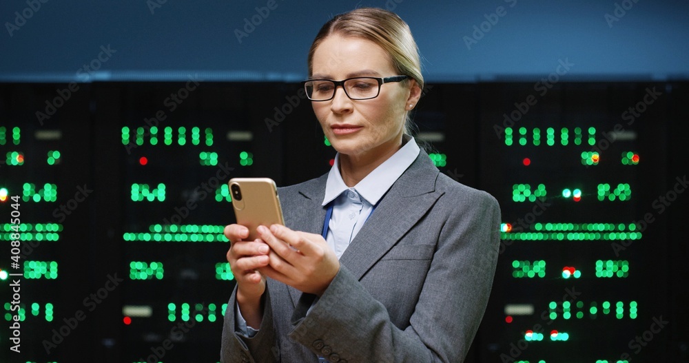 Beautiful female IT programmer with glasses stands in server room ...