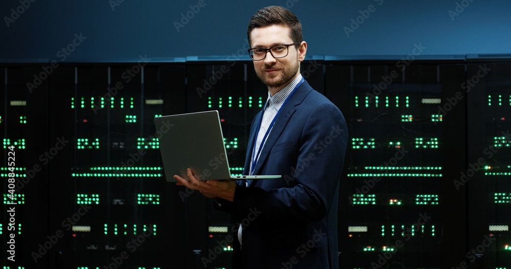 Portrait of IT worker with glasses standing in server room holding ...