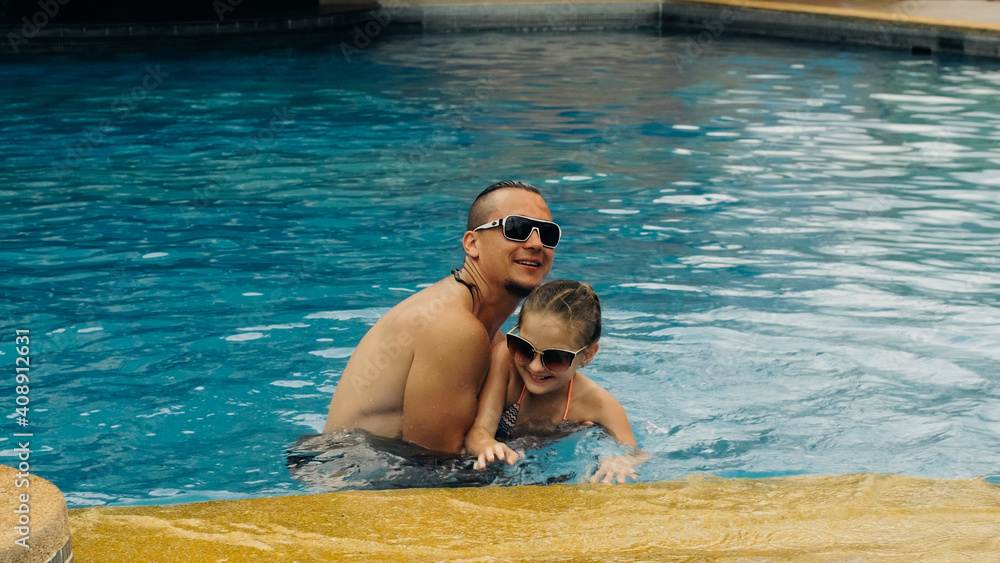 The father with little daughter have fun in the pool. Dad plays with ...
