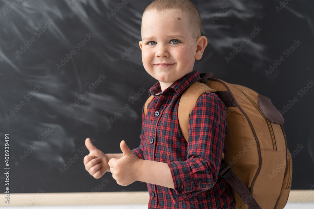 Happy smiling boy stands at school near the blackboard. He shows the ...